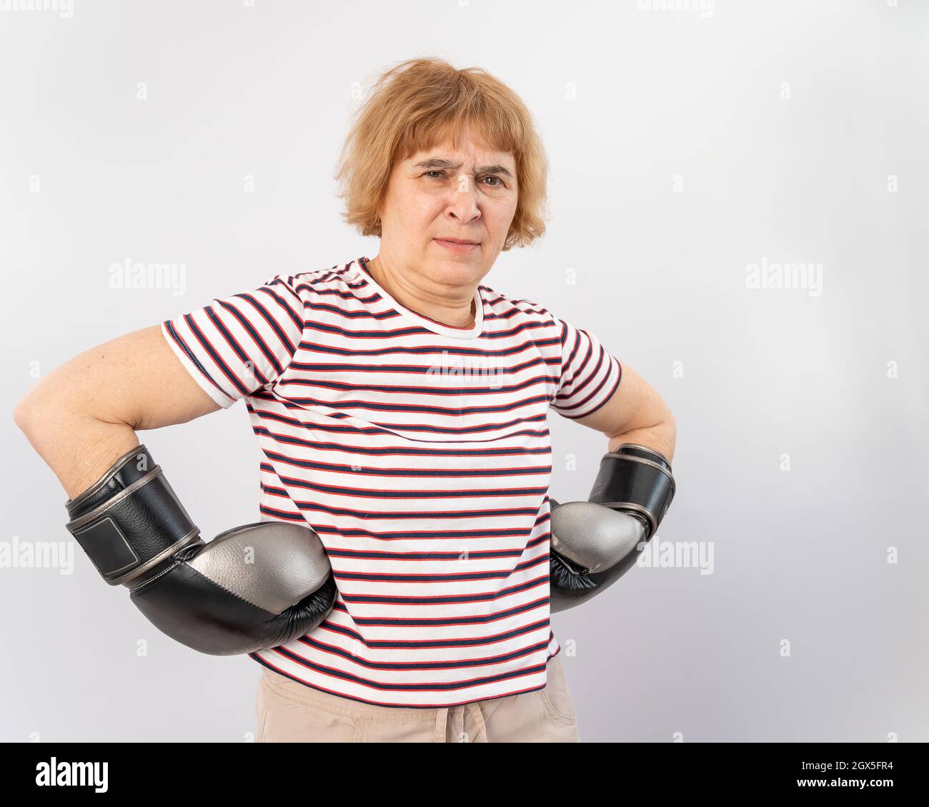 Elderly woman in fighting gloves in a defensive pose on a white ...