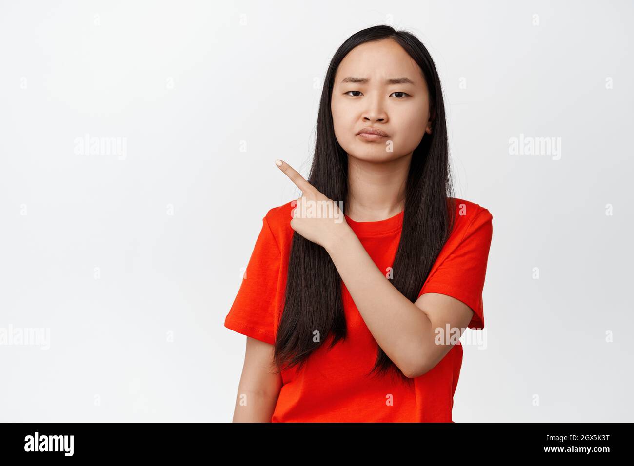 Sad asian girl pointing finger at upper left corner and complaining ...