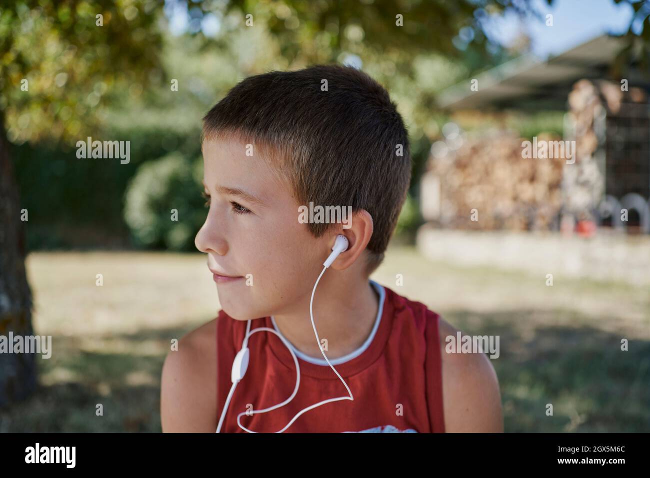 A cute boy listen to music while he looks away under s tree-shade. A ...