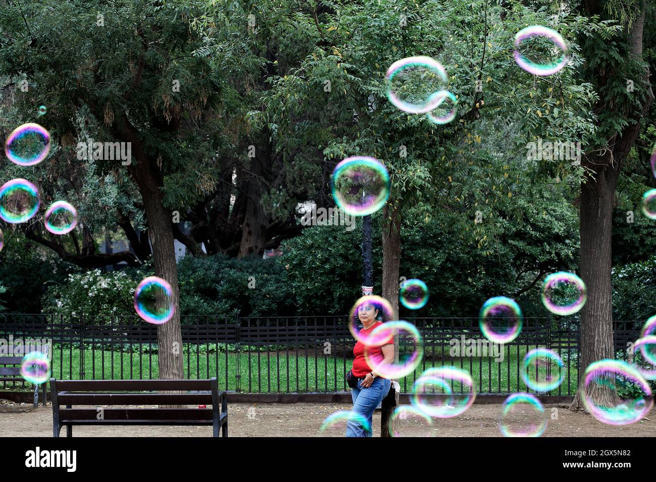 A woman leans against a tree watching soap bubbles fly gently past her ...