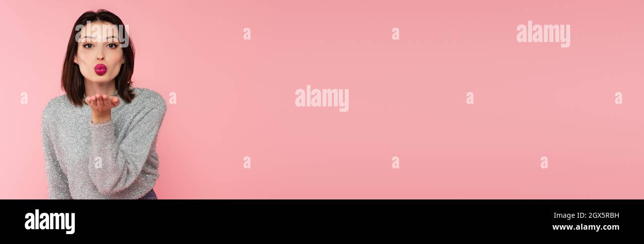 Pretty woman in sweater blowing air kiss at camera isolated on pink ...