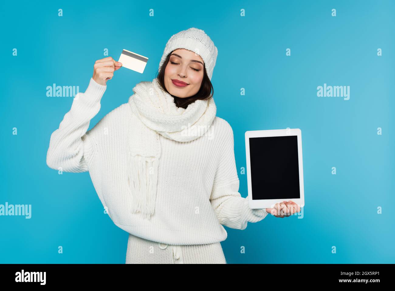 Smiling woman in cozy sweater and hat holding credit card and digital ...