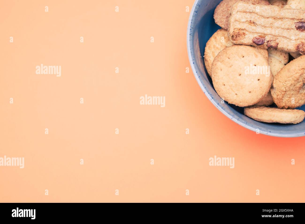 Vertical shot of organic biscuits in a blue bowl on orange surface with ...