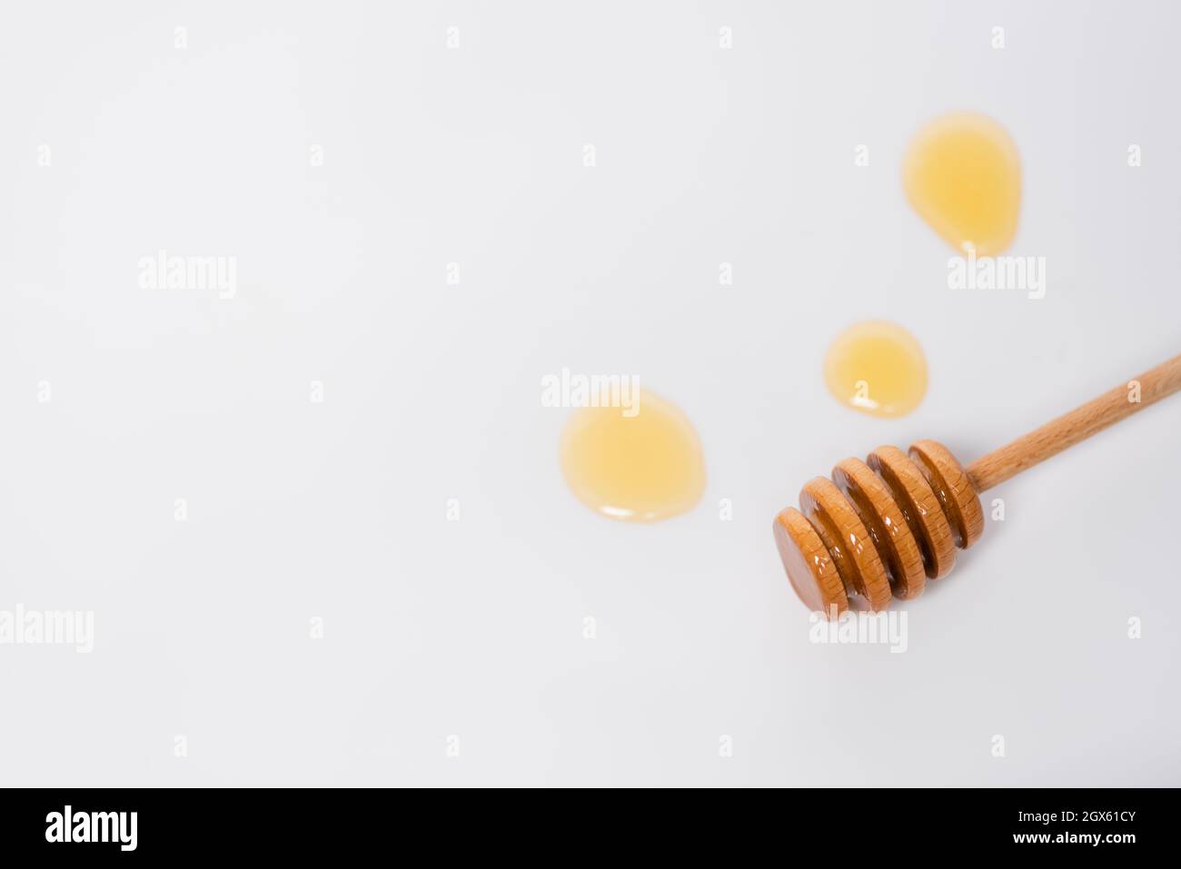 top view of wooden dipper near honey drops on white background with ...