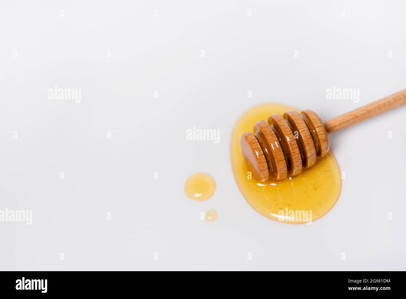 top view of wooden dipper near drops of honey on white background with ...