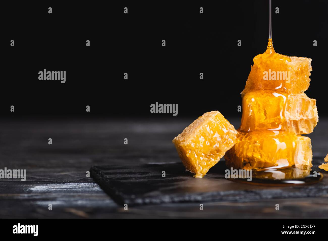 golden honey flowing on pieces of honeycomb on dark surface isolated on ...