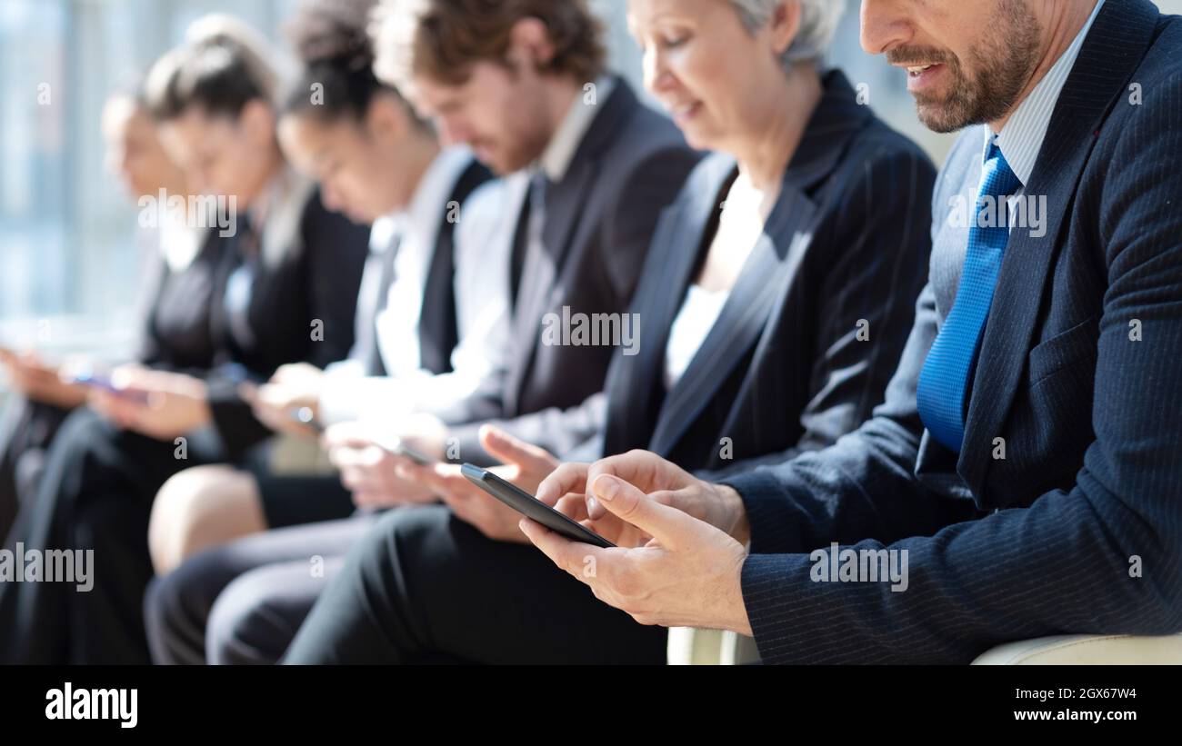 Diverse group of customers sitting in line, holding digital gadgets ...