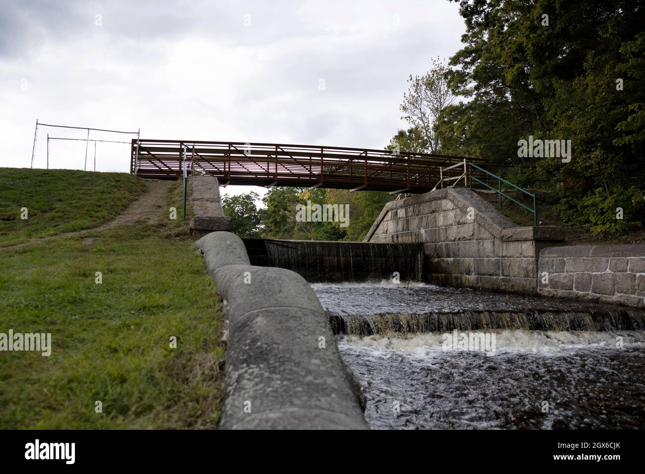A bridge crosses the dam spillway by the reservoir on a cloudy fall day ...