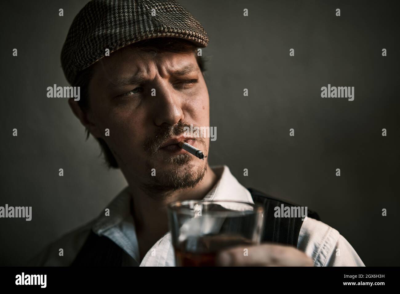 Young guy smoke a cigarette and drinks whiskey, blows smoke, dressed in ...