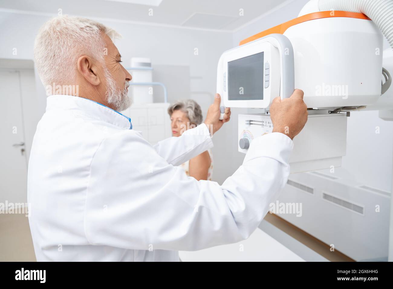 Old grey haired doctor using moving big ultrasound equipment looking at ...