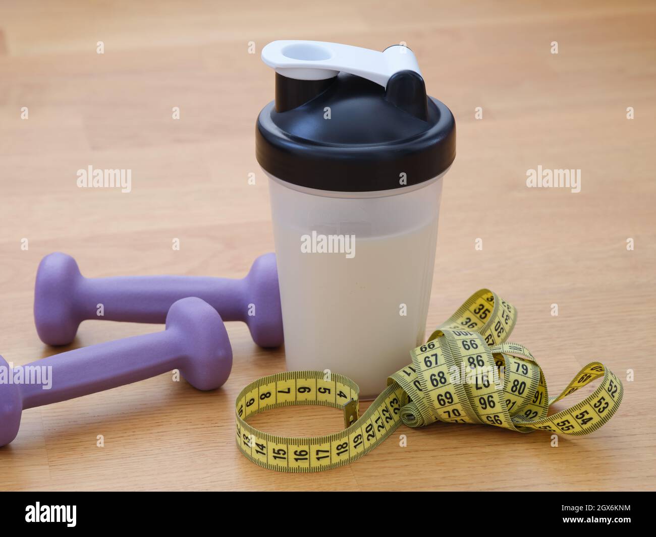 A protein shaker with a tape measure and weights near it. Close up ...