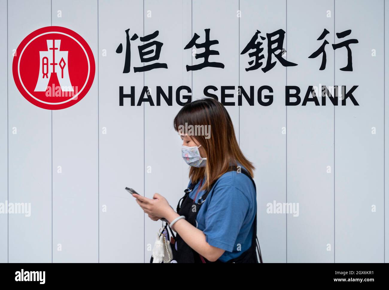 A woman wearing a face mask walks past the Hang Seng Bank branch and ...