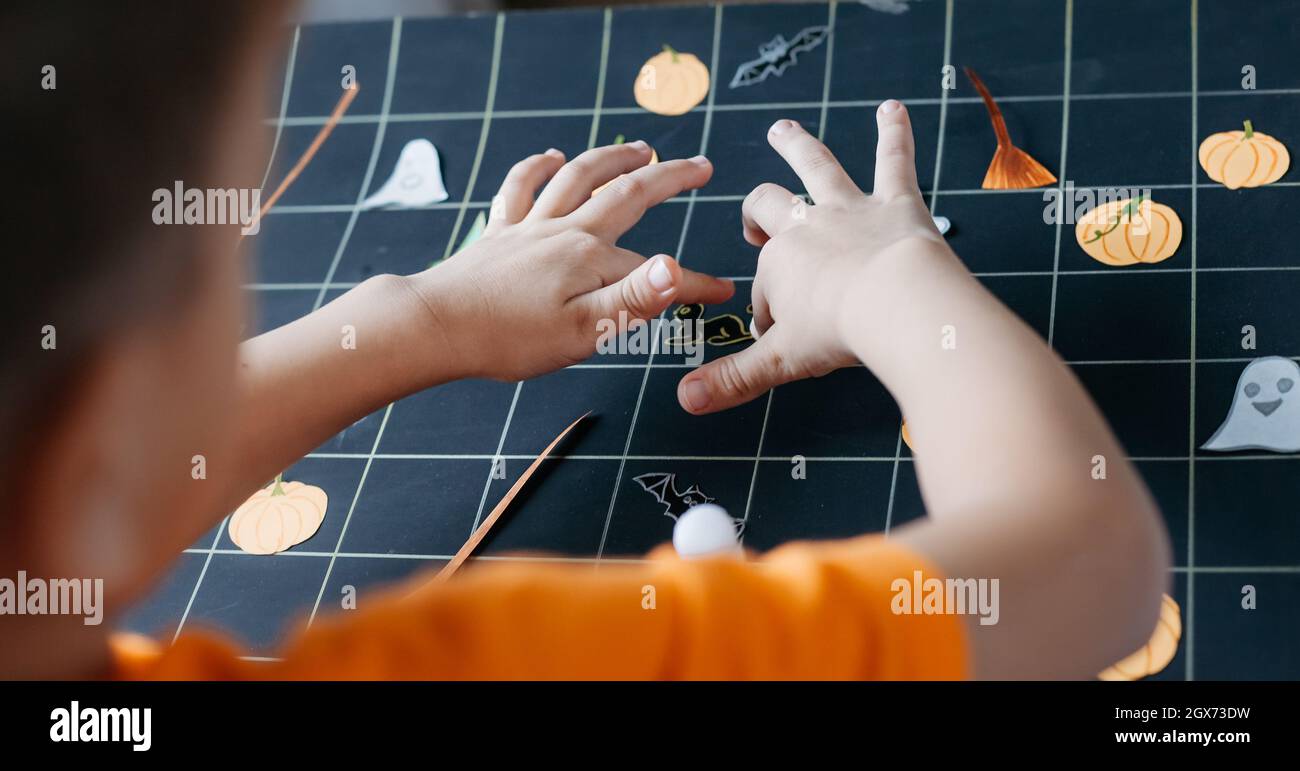 Cute child creating Halloween-themed board game. Boy gluing paper-cut ...