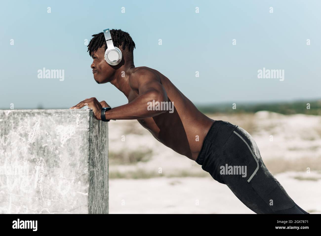 Sporty african black man, wearing wireless headphones, doing push-ups ...