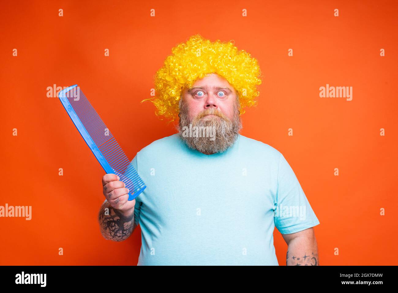 Fat amazed man with beard, tattoos and sunglasses combs himself with a ...