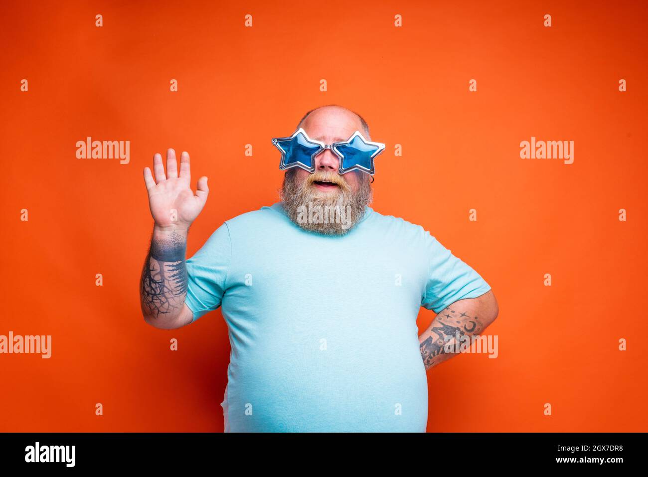 Fat happy man with beard, tattoos and sunglasses makes hello gesture ...