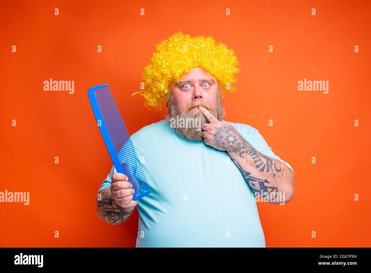 Fat thoughtful man with beard, tattoos and sunglasses combs himself ...