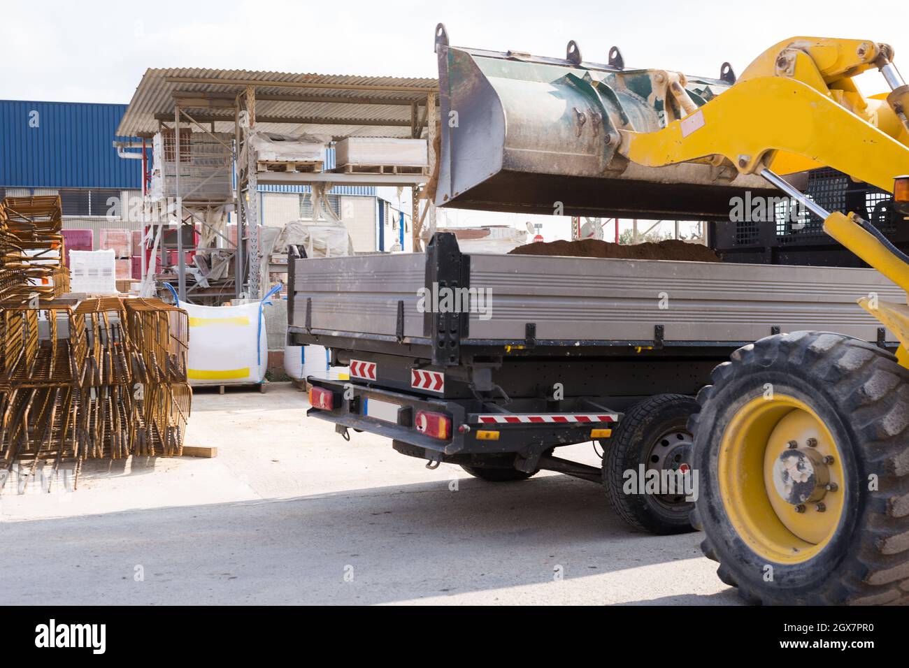 Excavator moving sand to empty truck at hardware store Stock Photo - Alamy