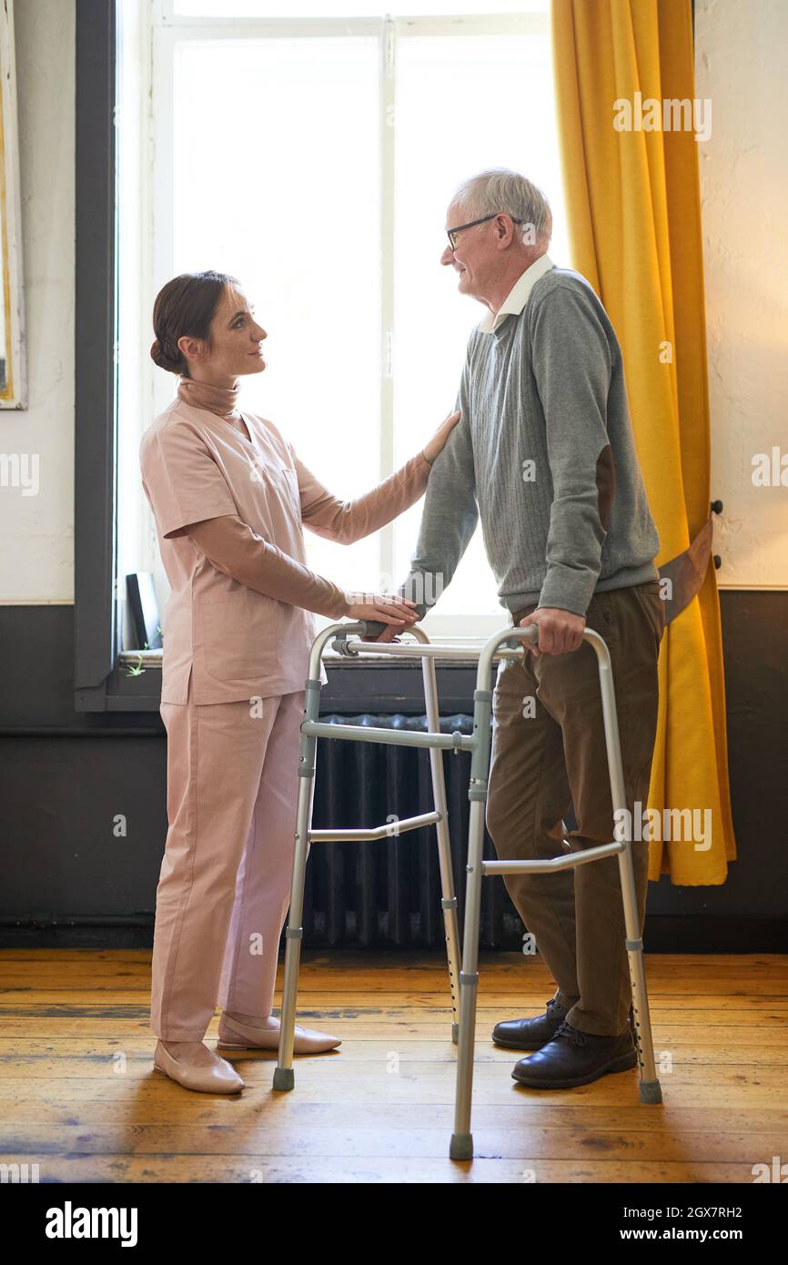 Vertical full length portrait of smiling young woman assisting senior ...