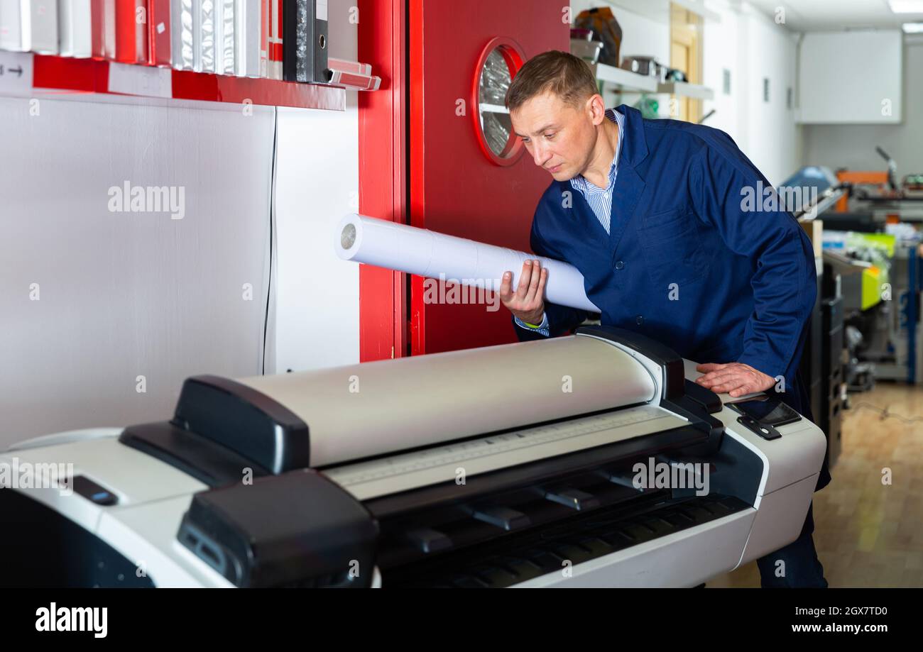 Worker loads new roll of paper into the plotter Stock Photo - Alamy