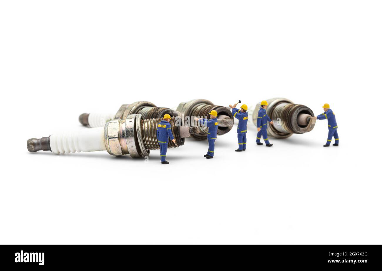 Miniature mechanic with old used engine spark plugs on white background ...