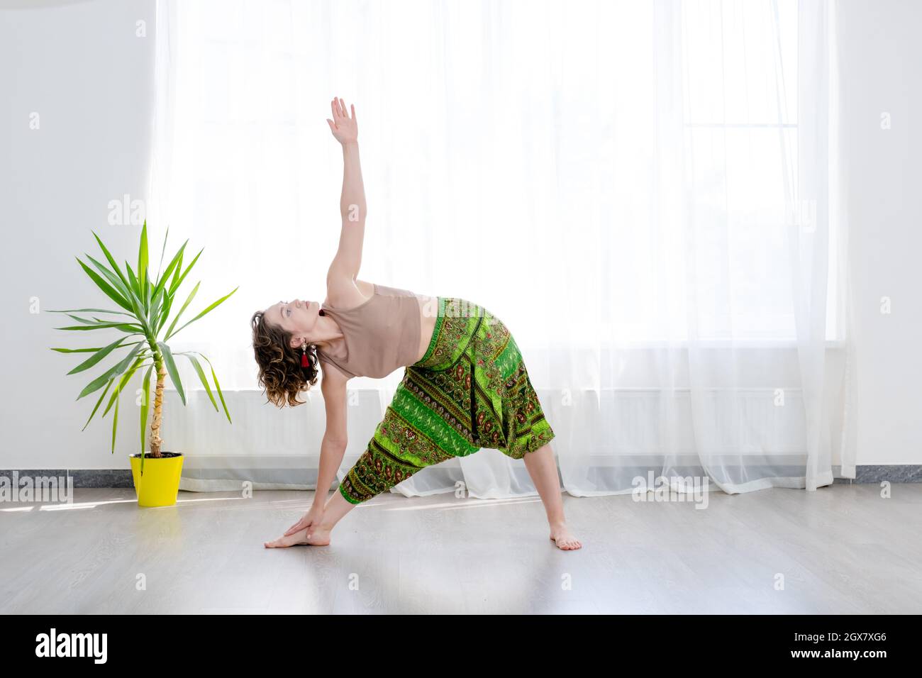 Young woman practicing yoga, standing in Utthita Trikonasana exercise ...