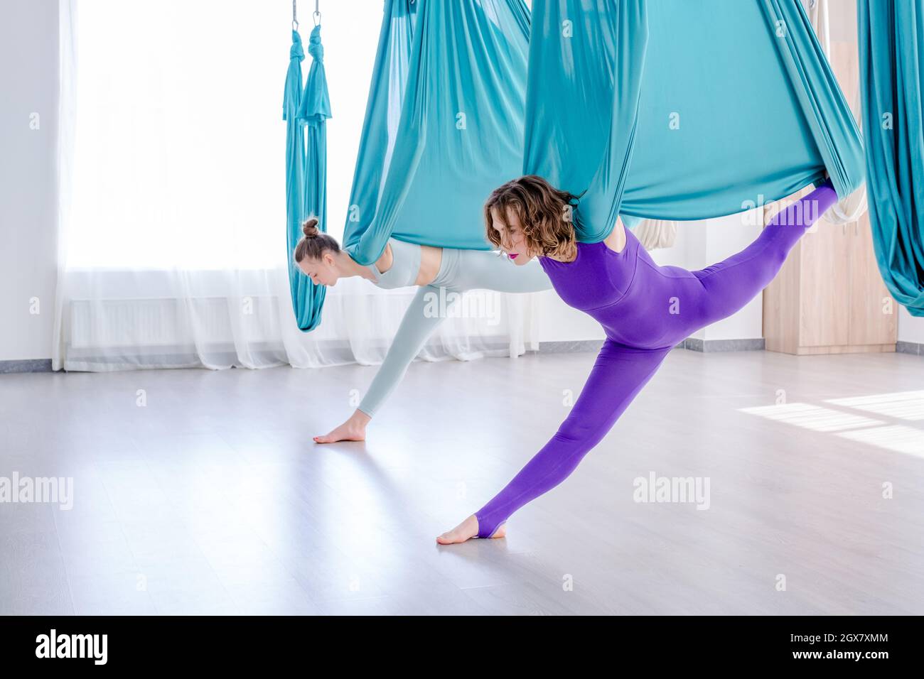 two women doing stretching exercises using fly yoga in fitness training ...