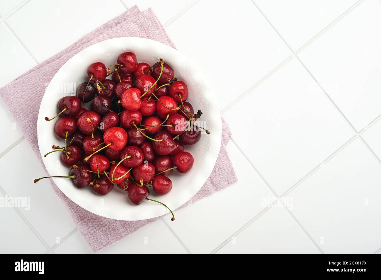 Cherry with water drops on heart shaped plate on white stone table ...