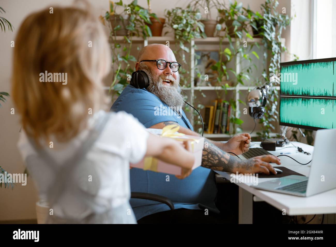 Cute little girl gives present to surprised dad working on computer in ...