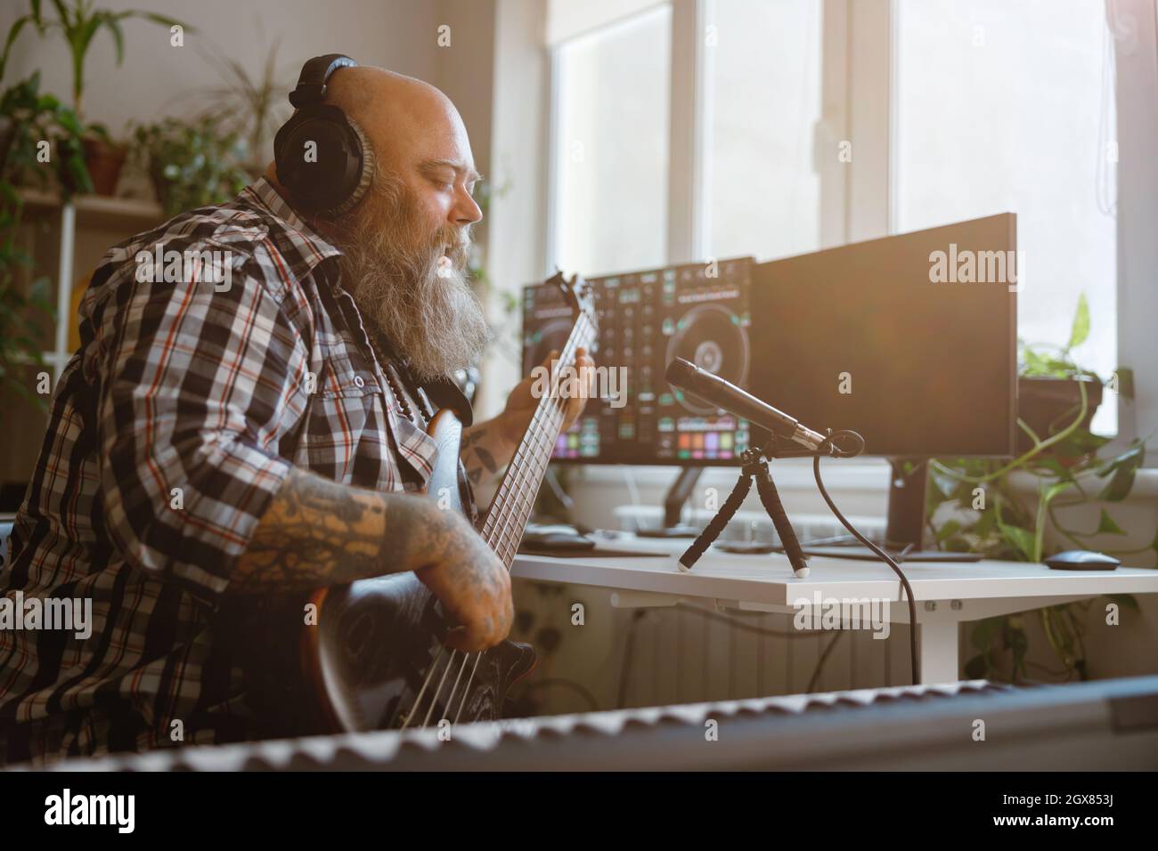 Mature composer plays bas guitar recording track at workplace in home ...