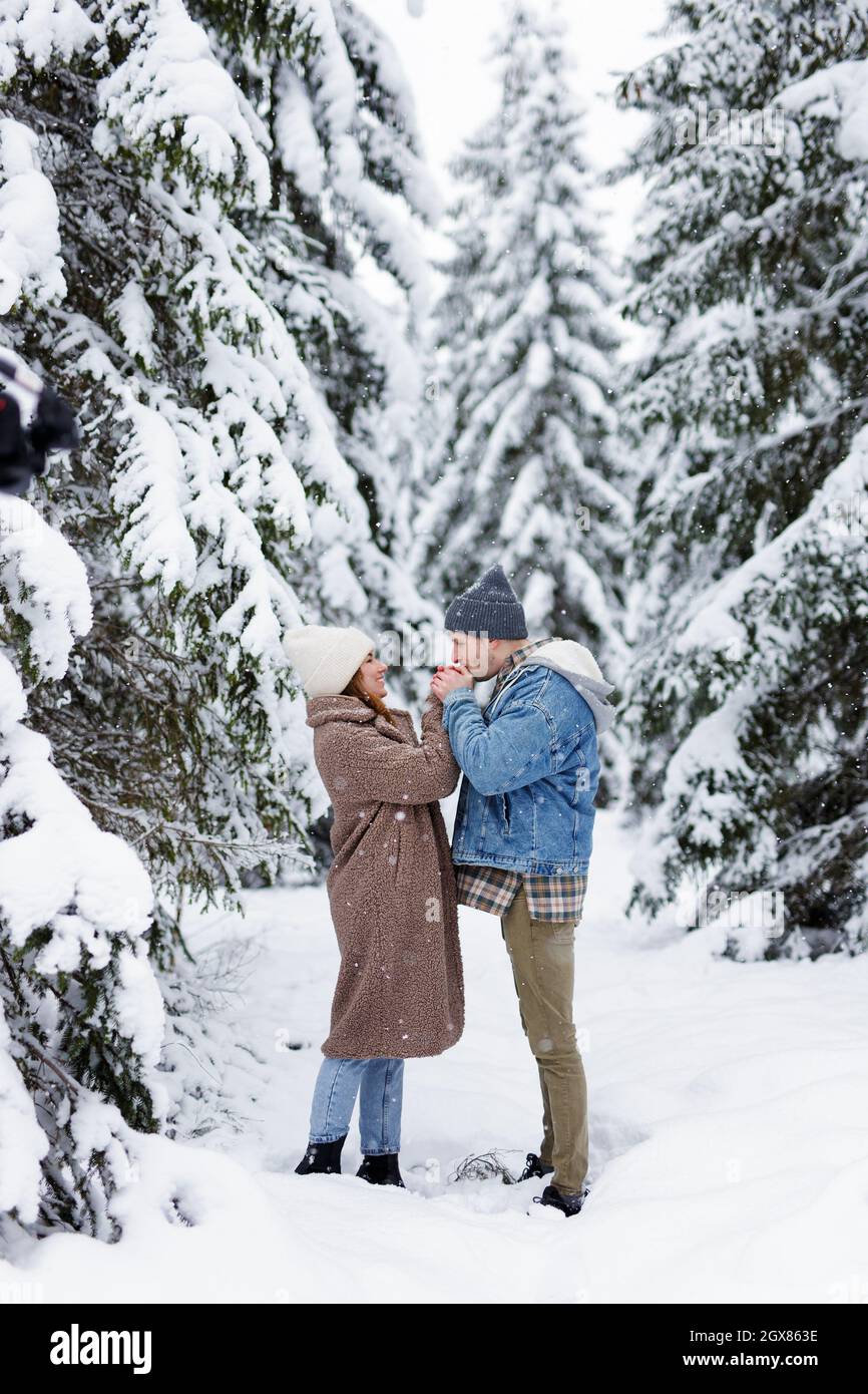 young cute couple standing in winter forest, holding hands and blowing ...