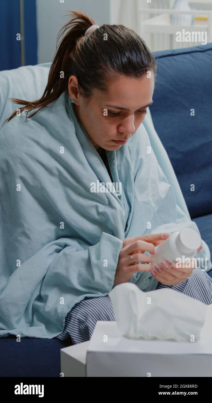 Sick woman reading label on bottle of pills and medicaments to cure ...