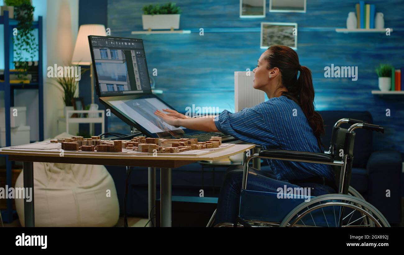 Engineer with disability using touch screen for building model at office. Invalid architect in ...