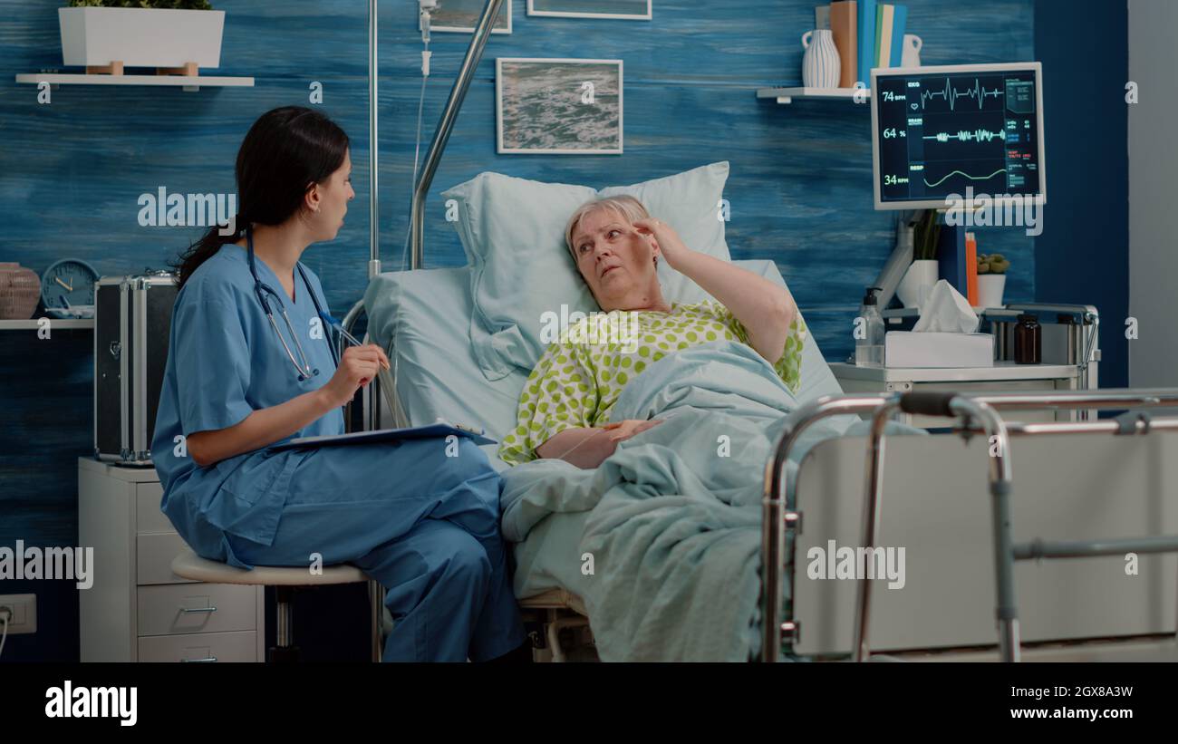 Medical assistant talking to senior patient with disease in bed about ...