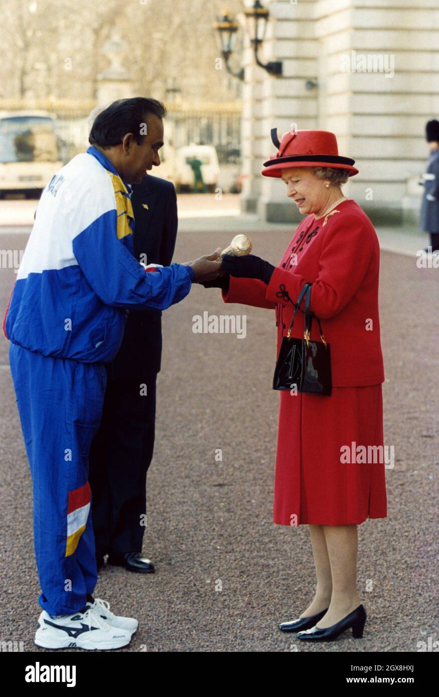 The Queen hands over a silver and gold baton to a Malaysian athlete ...