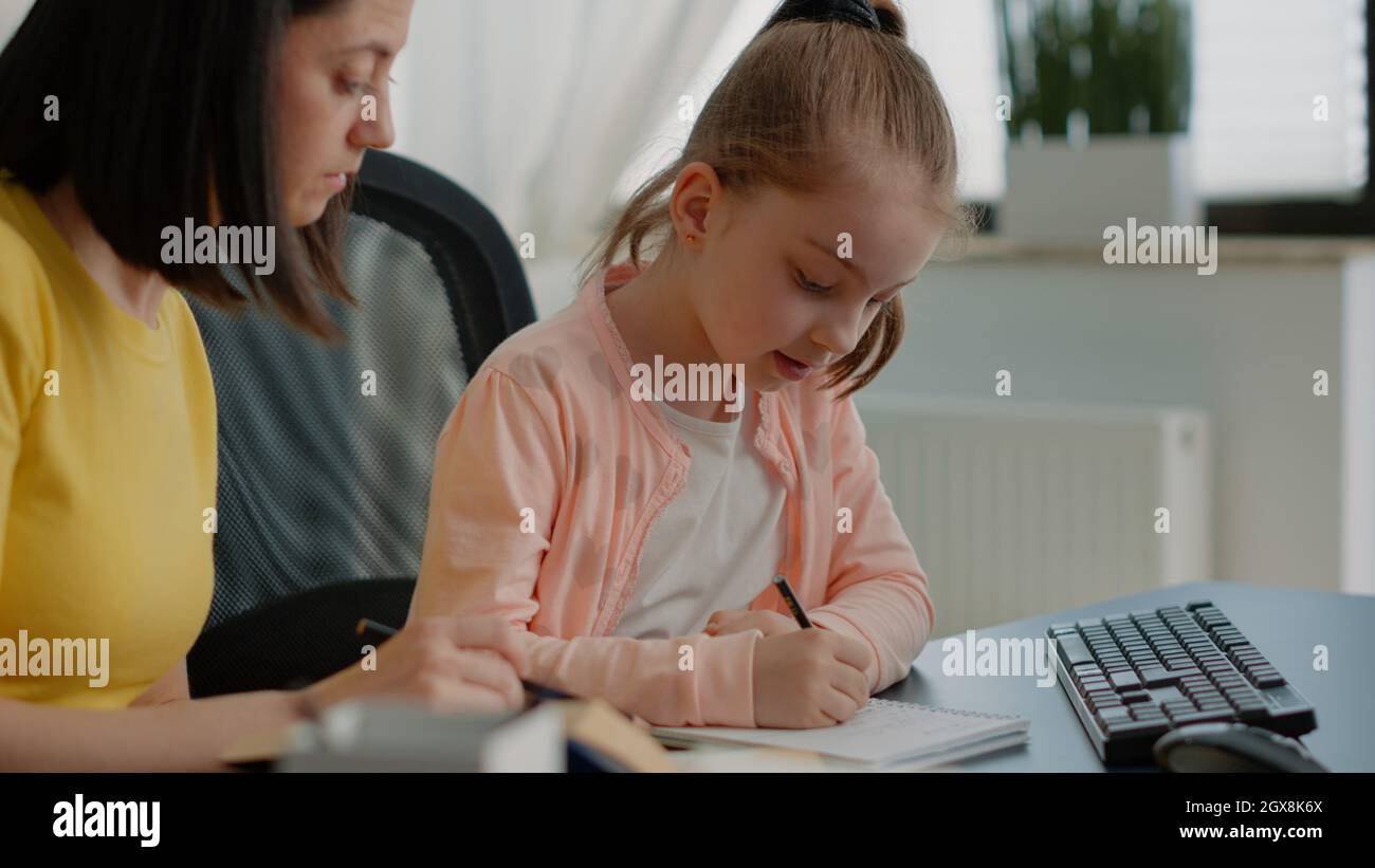 Young child writing homework on notebook and mother assisting for ...