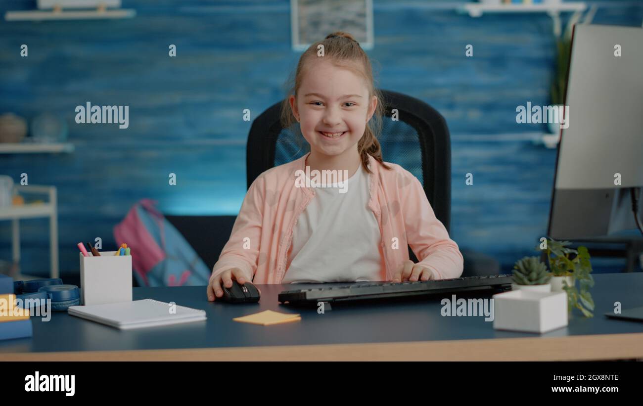 Portrait of schoolgirl at desk using computer and keyboard for online ...
