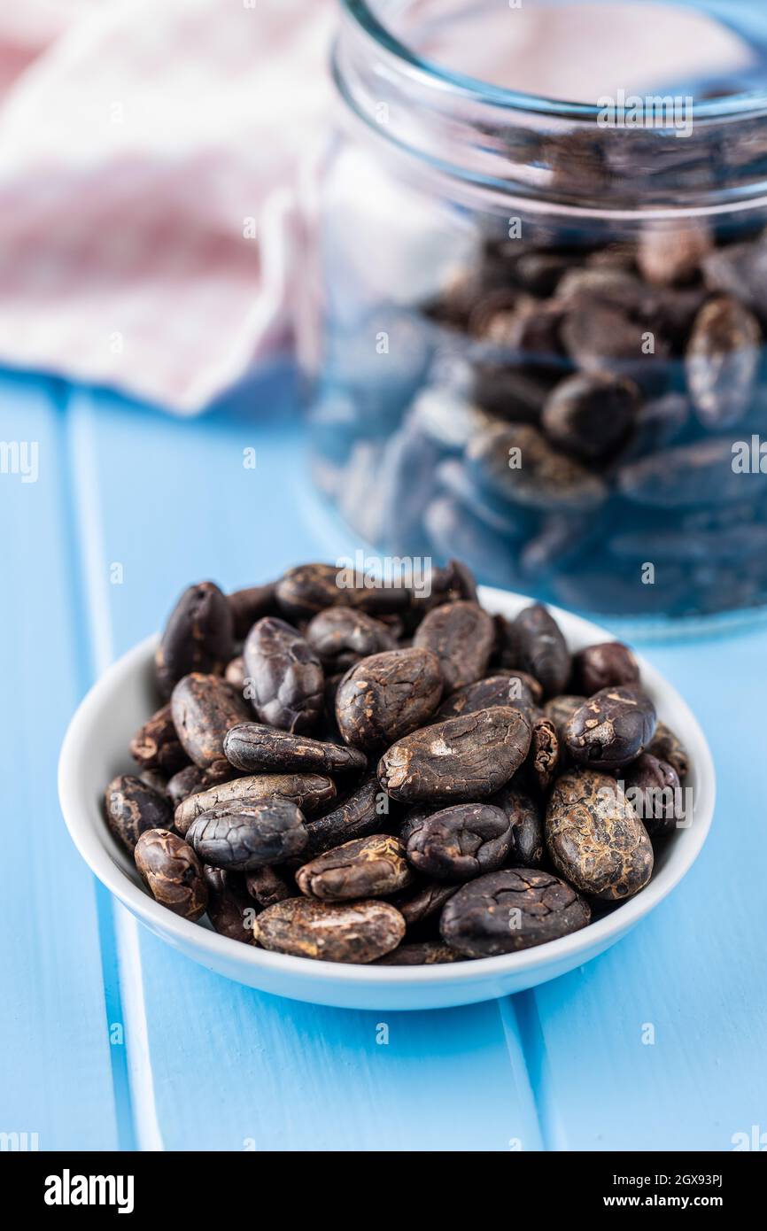 Roasted cocoa beans in bowl on blue table Stock Photo - Alamy