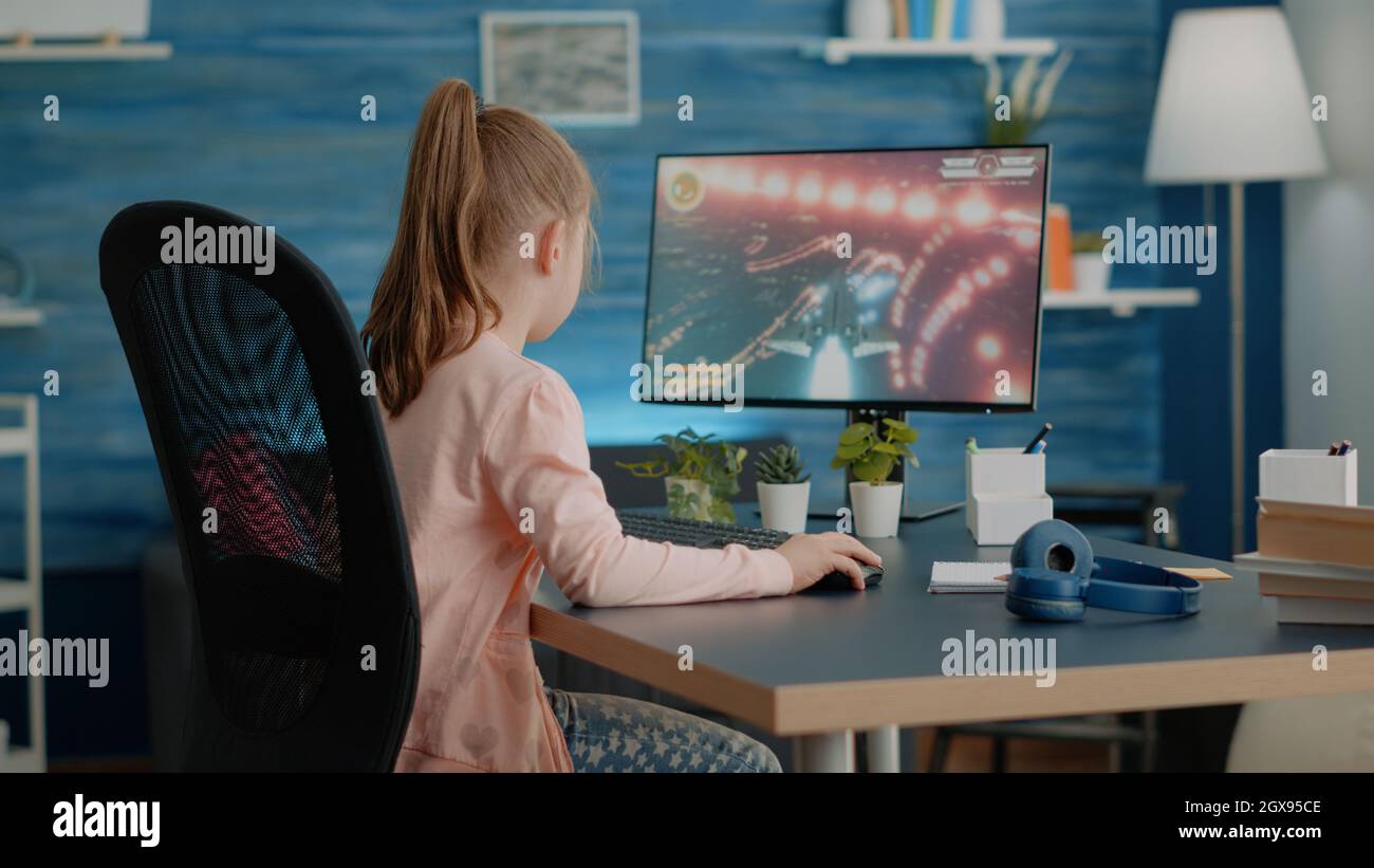 Young child playing action video games on computer at desk. Little girl ...