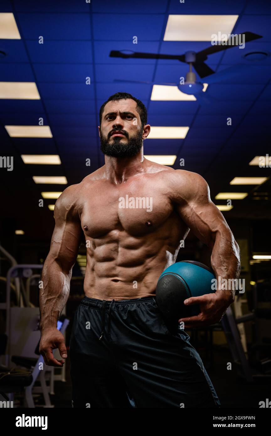 strong young bearded athlete with medicine heavy ball in blue lit night ...