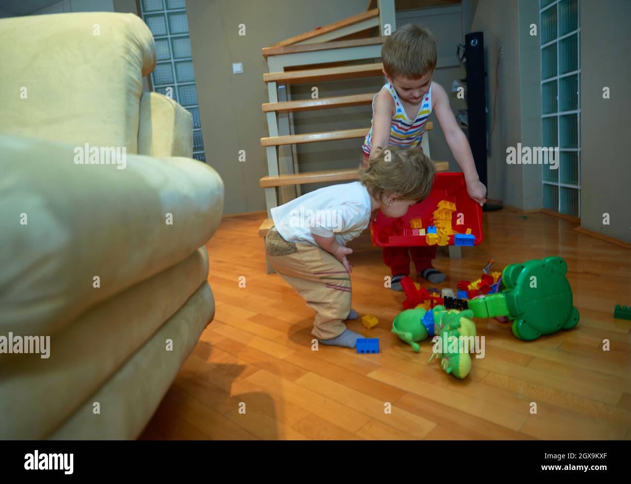 Little child playing at home and bring toys over stairs to his sister ...
