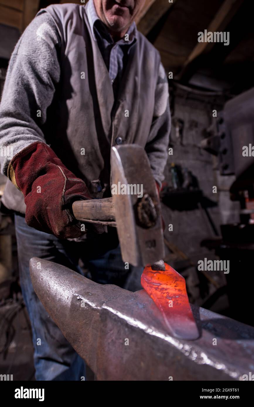 blacksmith manually forging the red hot molten metal on the anvil in ...