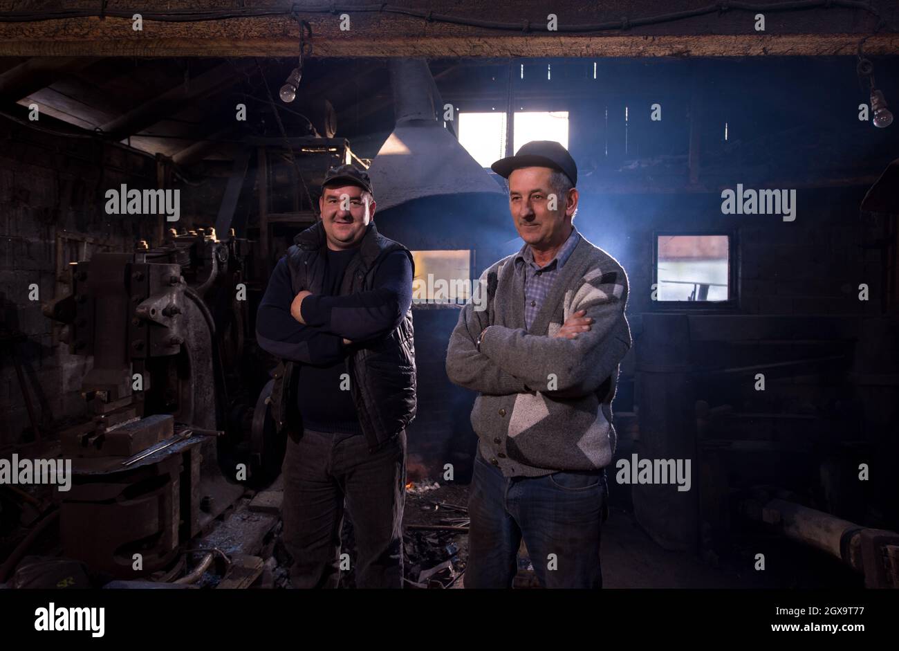 portrait of two generations confident blacksmith standing with crossed ...