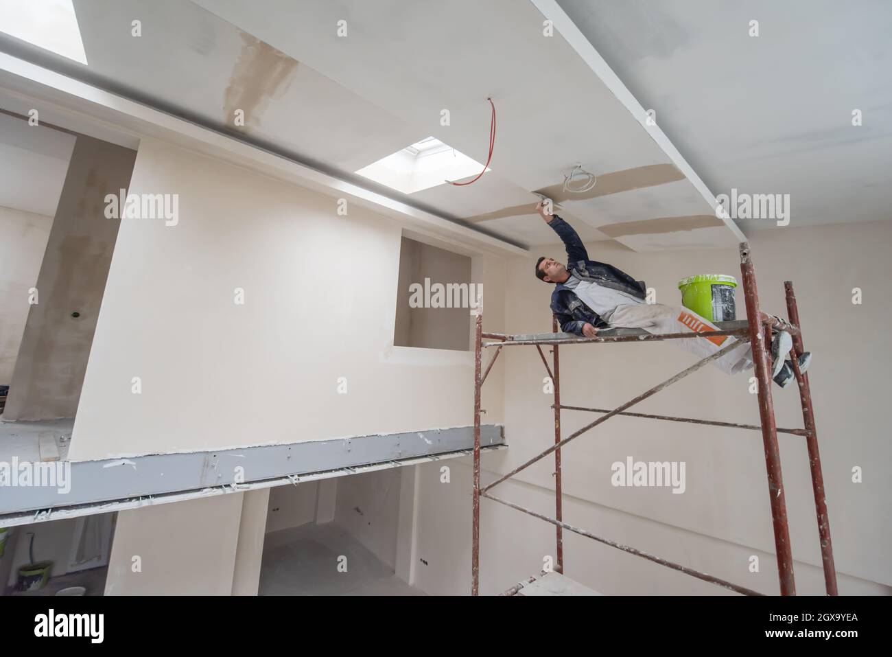 young professional construction worker using scaffold while plastering ...