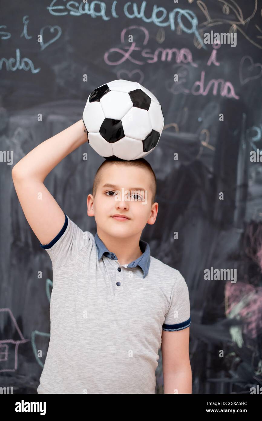 portrait of happy cute boy having fun holding a soccer ball on his head ...