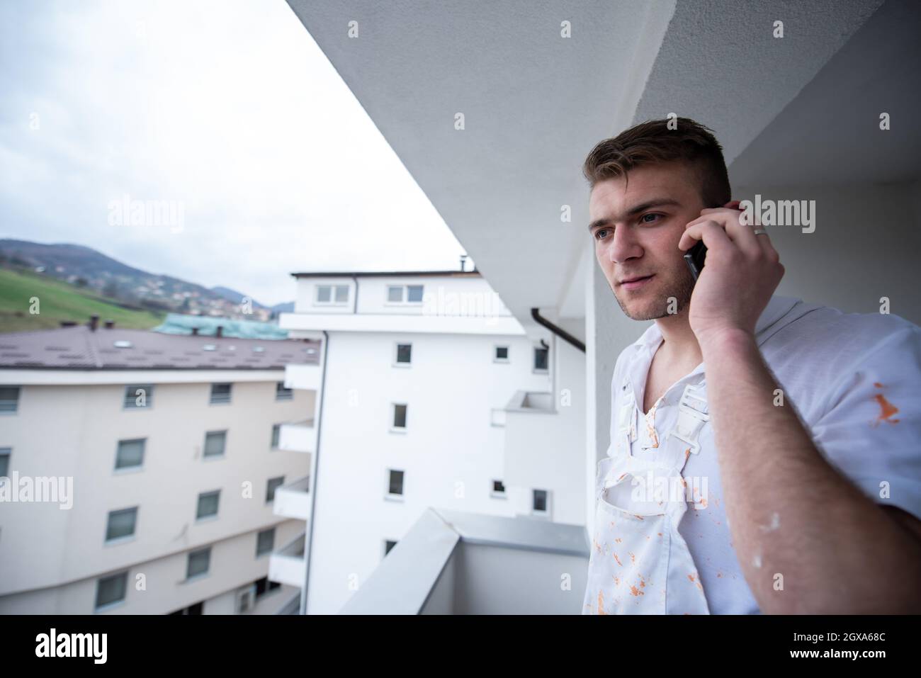 Painter making telephone call while standing on balcony during break ...