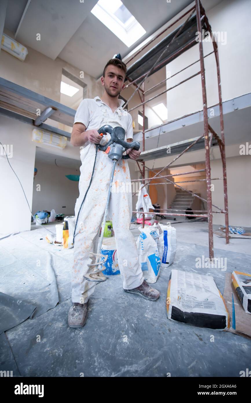 professional Male builder mixing plaster in bucket using electric mixer ...