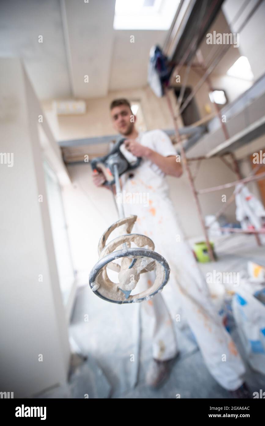 professional Male builder mixing plaster in bucket using electric mixer ...