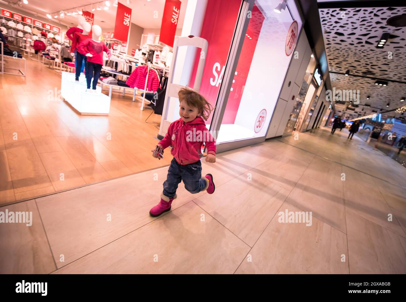 a little happy cute girl running in front of the store in the shopping ...