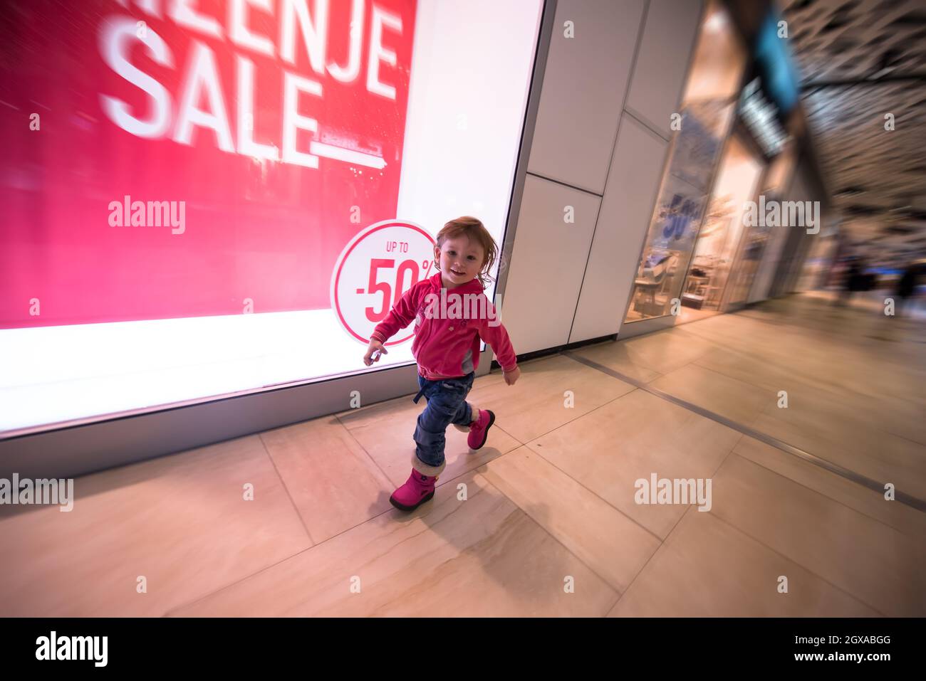a little happy cute girl running in front of the store in the shopping ...